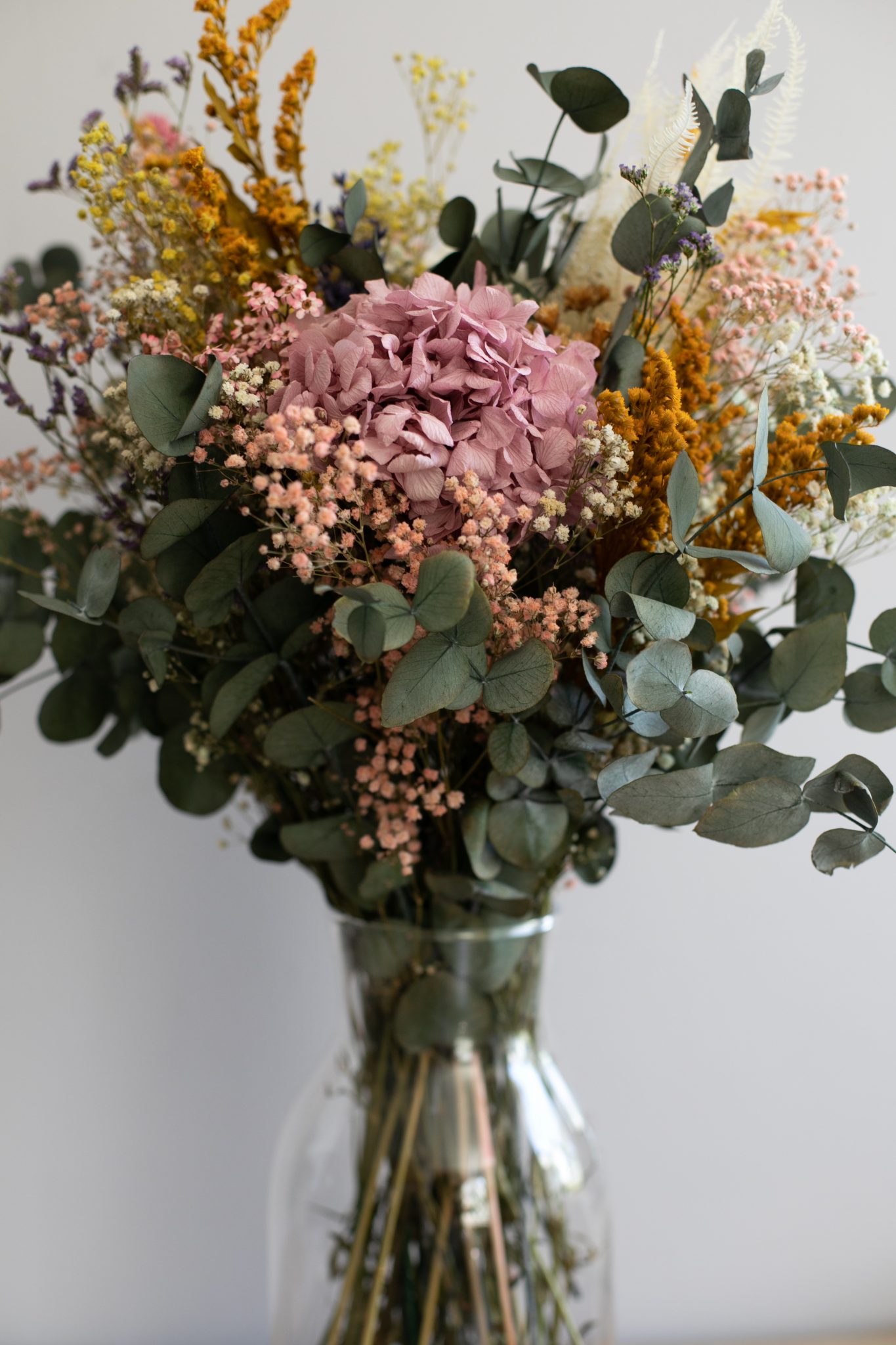 Jarrón alto de cristal con eucalipto, hortensia y flores preservadas